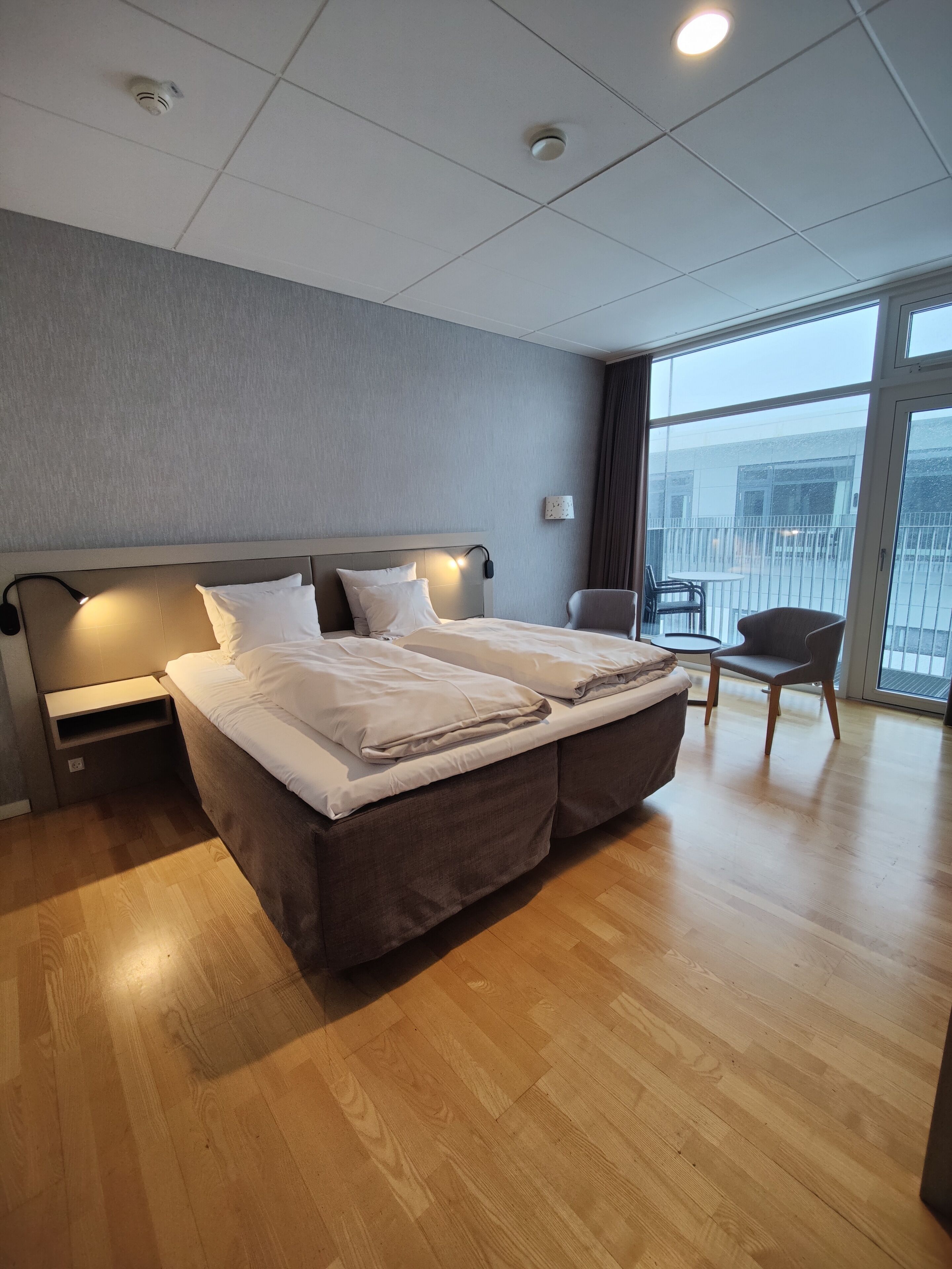 Quarto de hotel moderno com uma cama grande, uma cadeira, uma mesinha e uma varanda com vista.