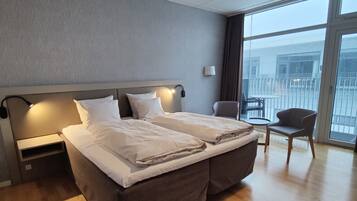 Quarto de hotel moderno com uma cama grande, uma cadeira, uma mesinha e uma varanda com vista.