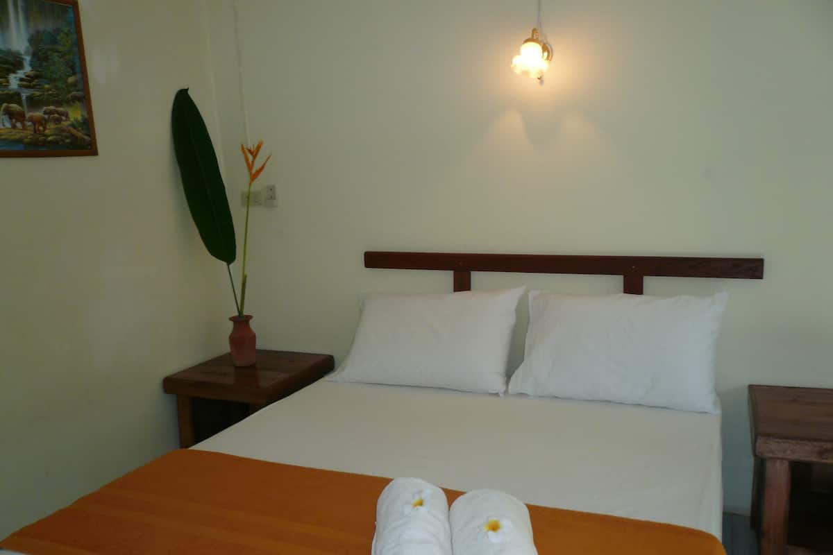 Cama bem arrumada com almofadas brancas e cabeceira de madeira, mesa de cabeceira pequena com uma planta e um quadro na parede.