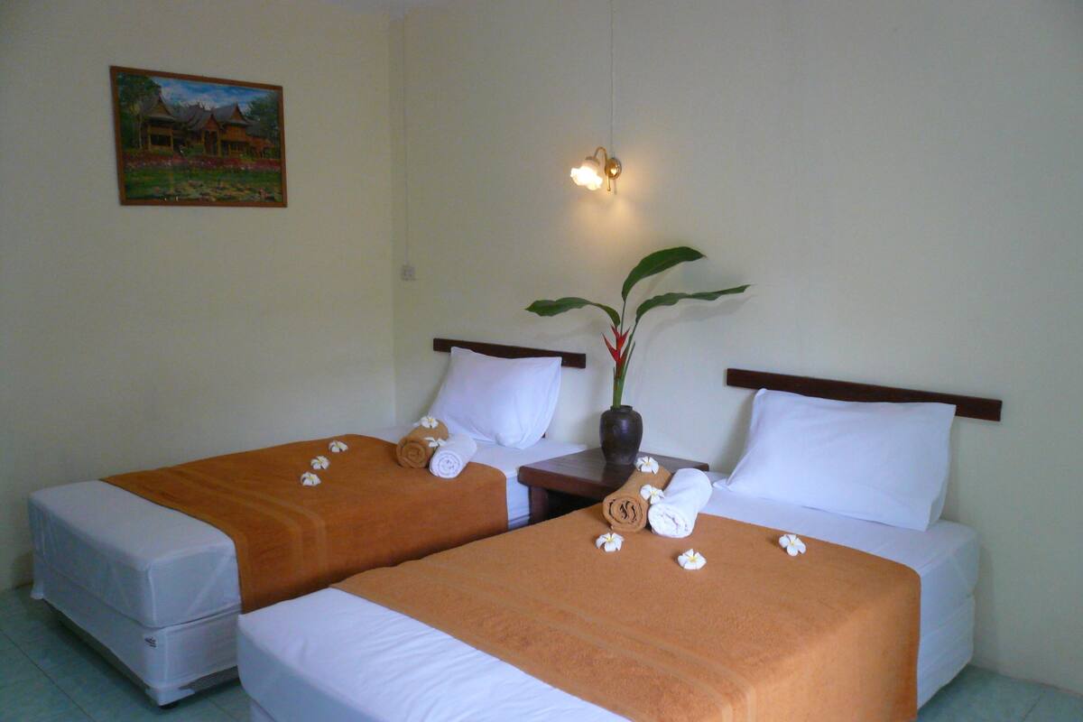 Duas camas de casal com roupa de cama marrom e branca, um vaso com uma planta e um quadro na parede.