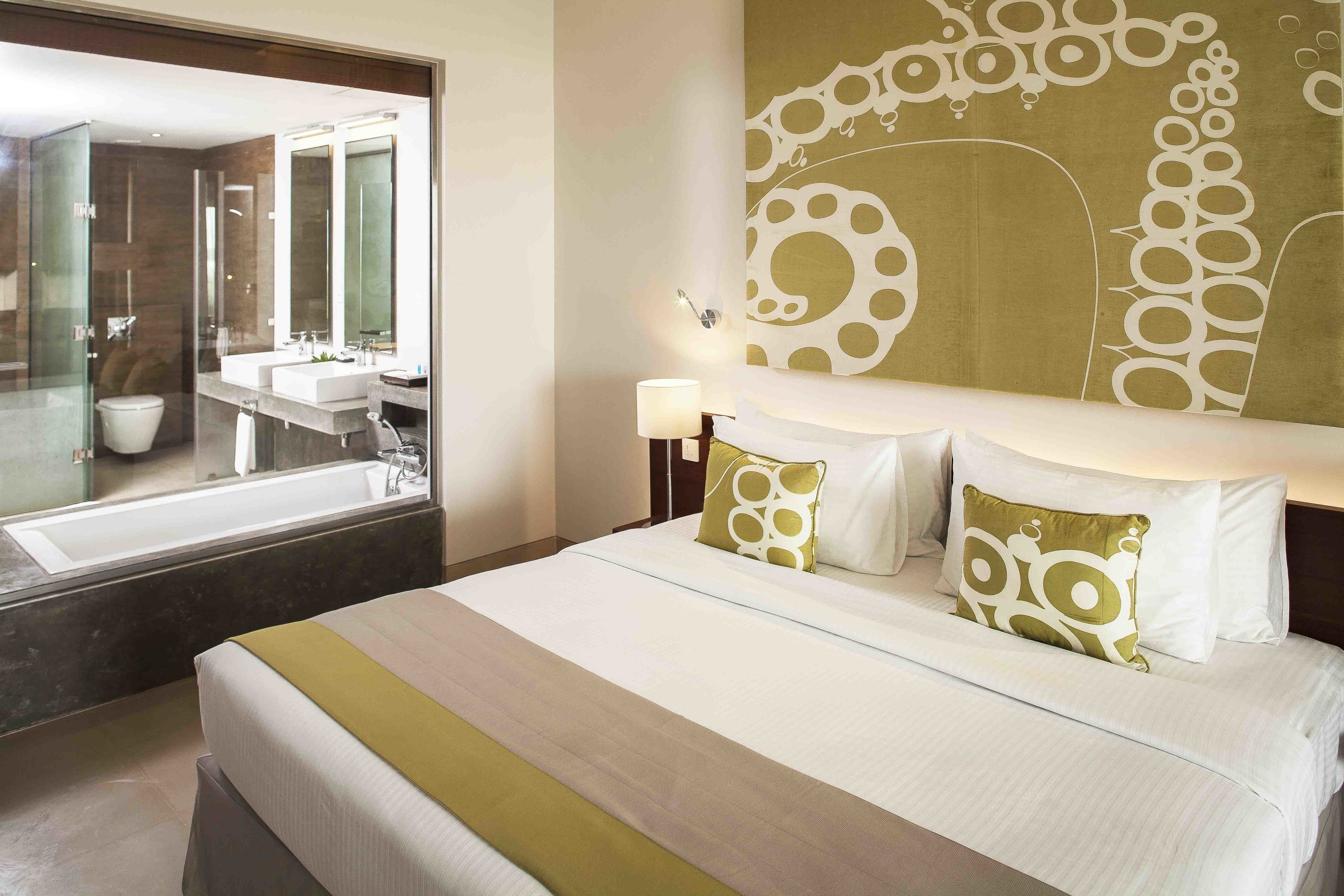 Quarto de hotel com uma cama grande, banheiro com banheira e parede com desenho circular.