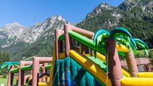 Uma estrutura inflável para brincar com escorregadores e elementos de escalada, com montanhas e céu claro ao fundo.