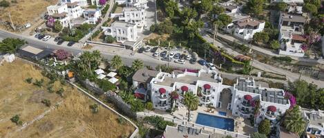 Vista aérea de uma área residencial com edifícios brancos modernos, piscina e estrada.