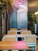 Interior de restaurante com um letreiro de neon que diz 'GOOD BEHAVIOUR' e móveis de vime.