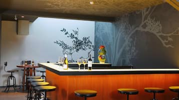 Uma área de bar com banquetas, um balcão com garrafas e copos, e uma parede com um mural de árvore.