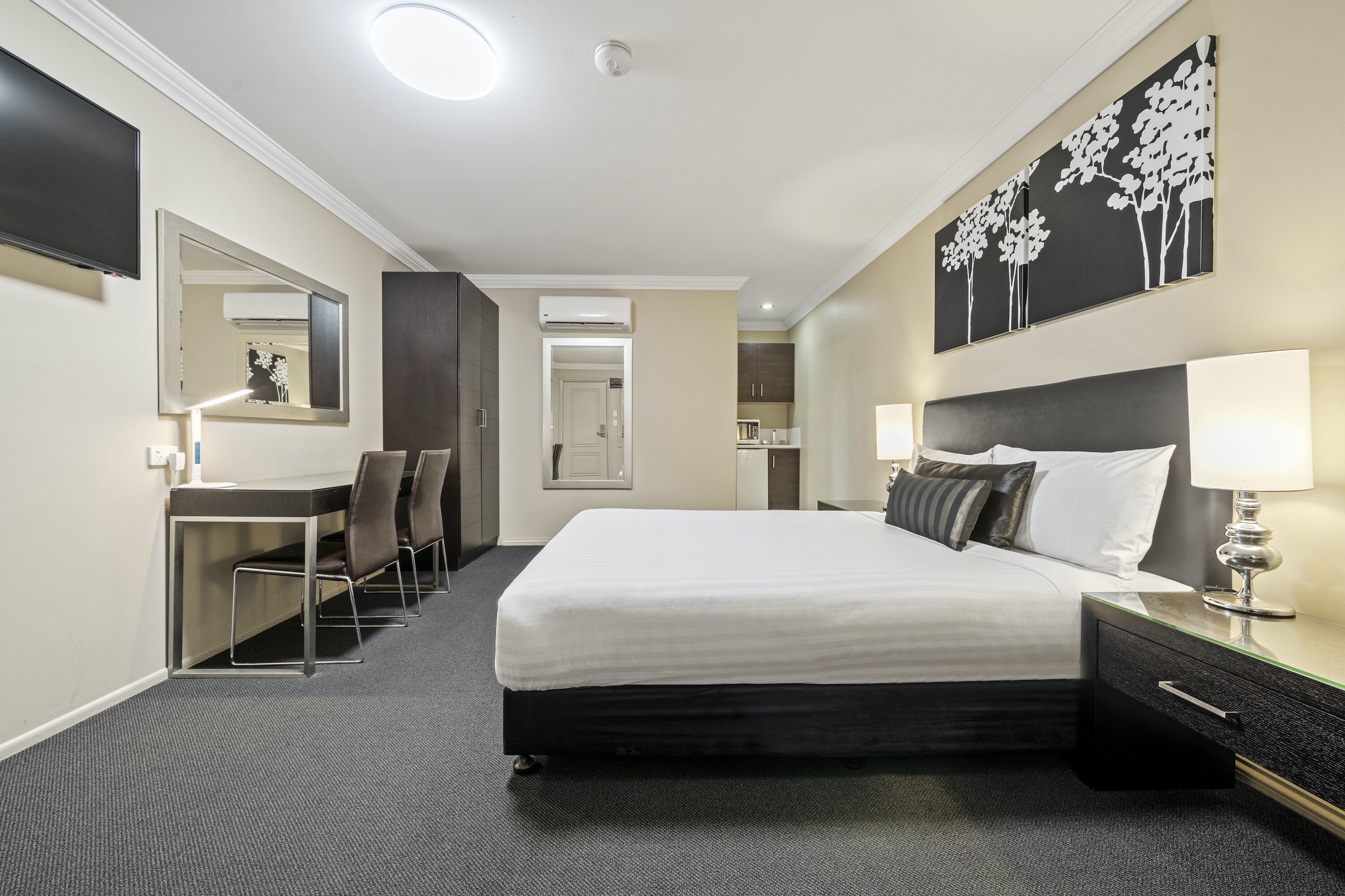 Quarto de hotel com uma cama grande, uma escrivaninha com cadeira, um espelho e uma televisão presa à parede.