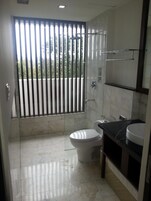 Casa de banho com sanita, lavatório, chuveiro e uma porta de vidro que dá para uma varanda.