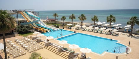 Área da piscina com toboáguas, cadeiras de descanso, guarda-sóis e vista para o oceano.
