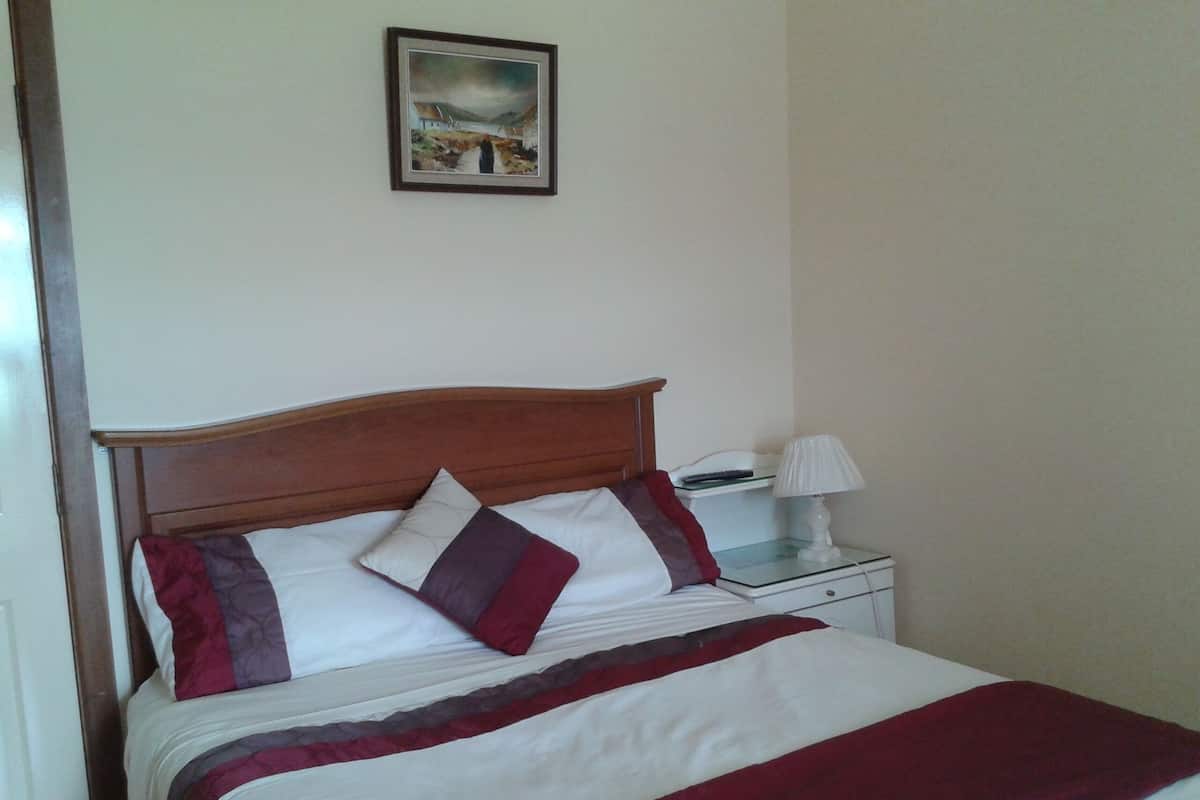 Uma cama bem arrumada com cabeceira de madeira, mesa de cabeceira com abajur e um quadro na parede.