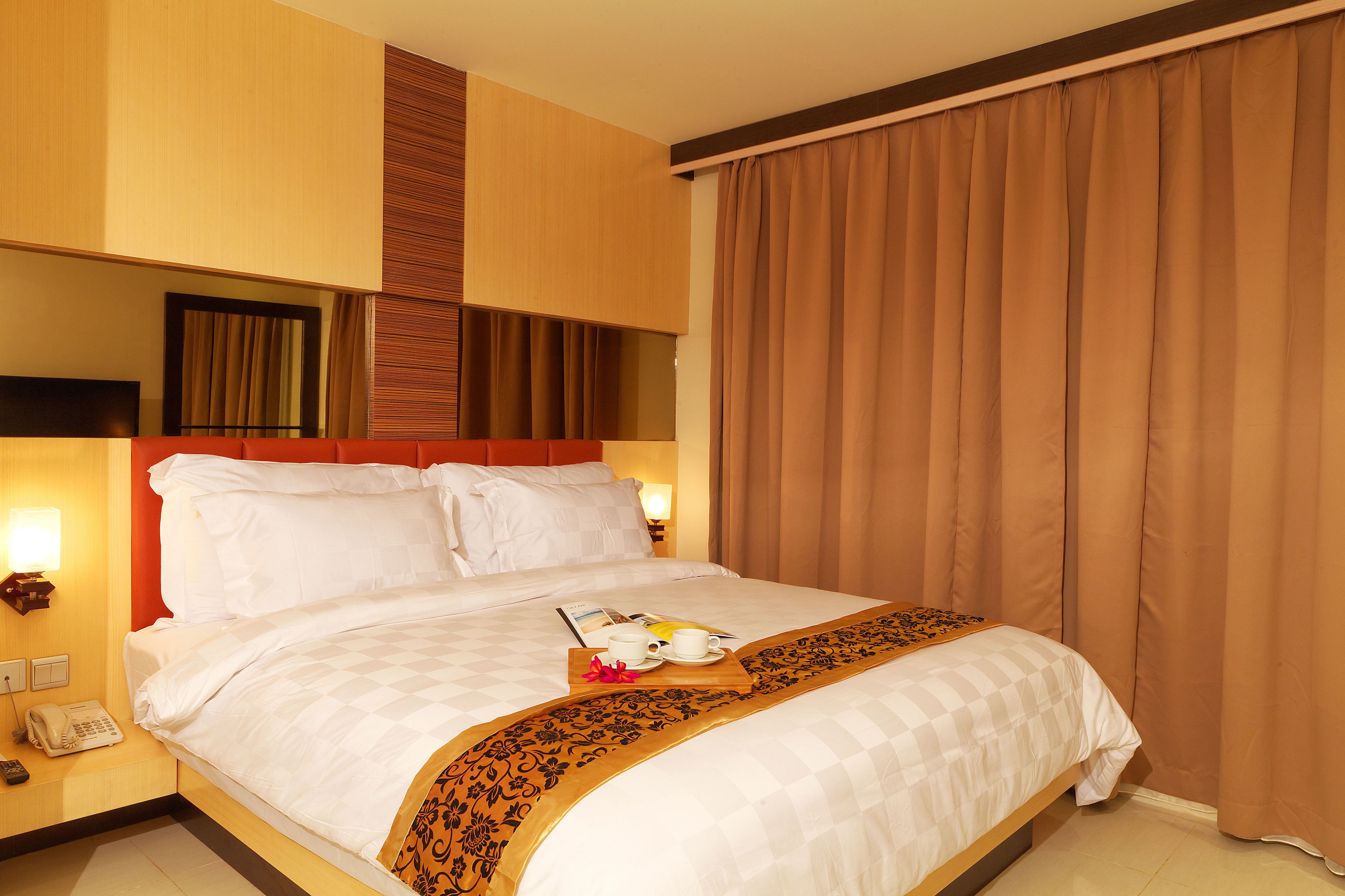 Quarto de hotel com uma cama grande, uma mesinha de cabeceira com telefone e uma janela com cortinas.
