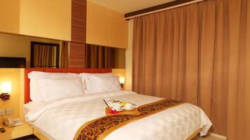 Quarto de hotel com uma cama grande, uma mesinha de cabeceira com telefone e uma janela com cortinas.