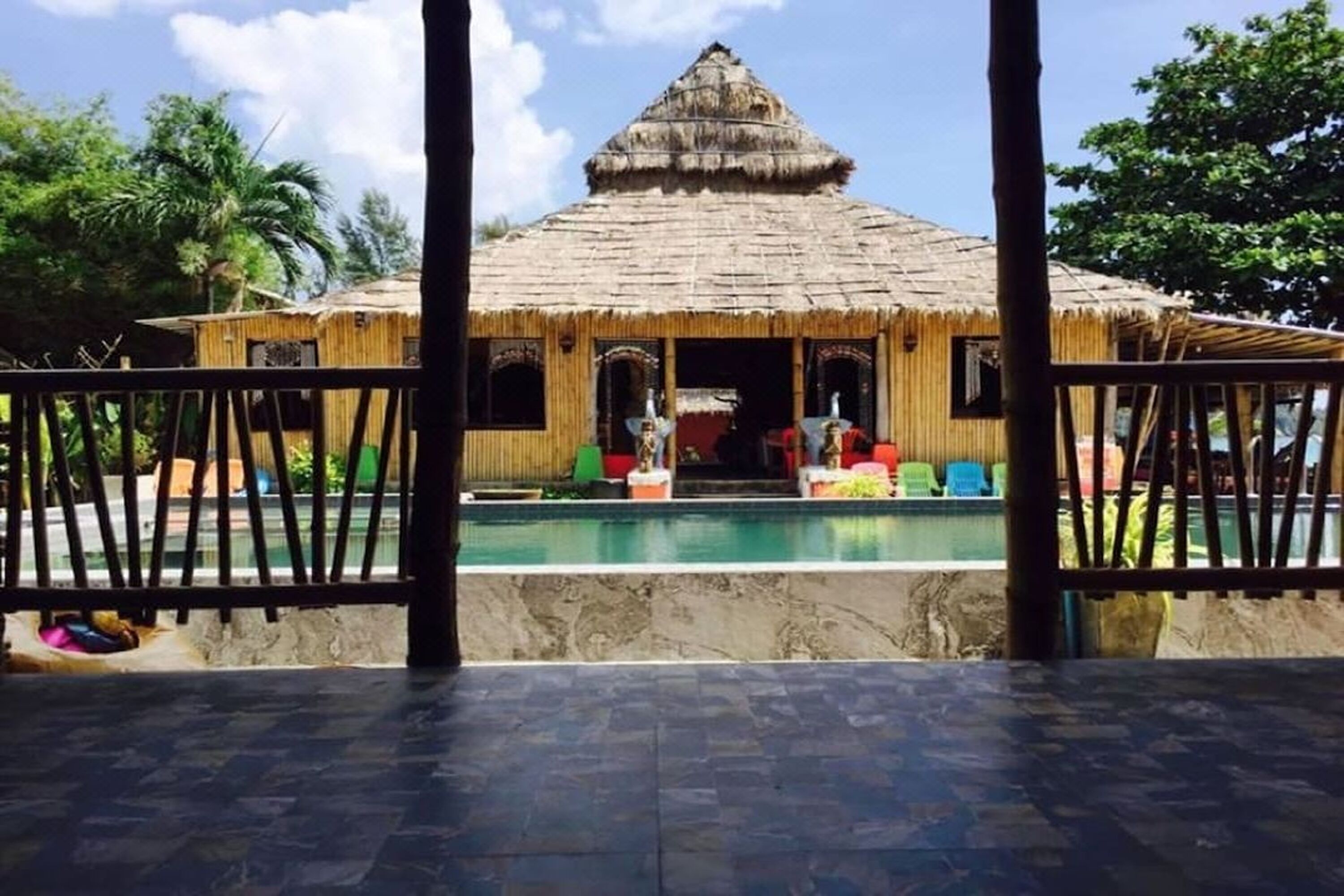 Uma construção com telhado de palha e uma piscina em primeiro plano.