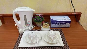 Uma mesa com uma chaleira elétrica branca, uma caixa de café MyDIN, uma pequena planta em vaso e duas xícaras de chá brancas sobre um descanso tecido.
