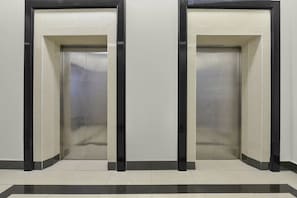 Duas portas de elevador em um corredor com piso de azulejos.
