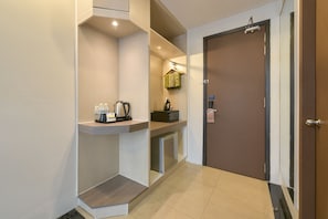 Quarto de hotel moderno com cozinha compacta, porta com placa 'Não Perturbe' e prateleira pequena com chaleira e garrafas.