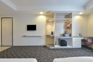 Quarto de hotel com cama, escrivaninha com cadeira, televisão, guarda-roupa e uma pequena prateleira com cafeteira.