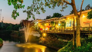 Restaurante à beira do rio com uma cascata, mesas ao ar livre e área coberta com vista para a água.