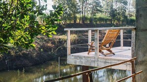 Um deck de concreto com uma cadeira e mesa de madeira, com vista para um corpo de água, rodeado por vegetação.