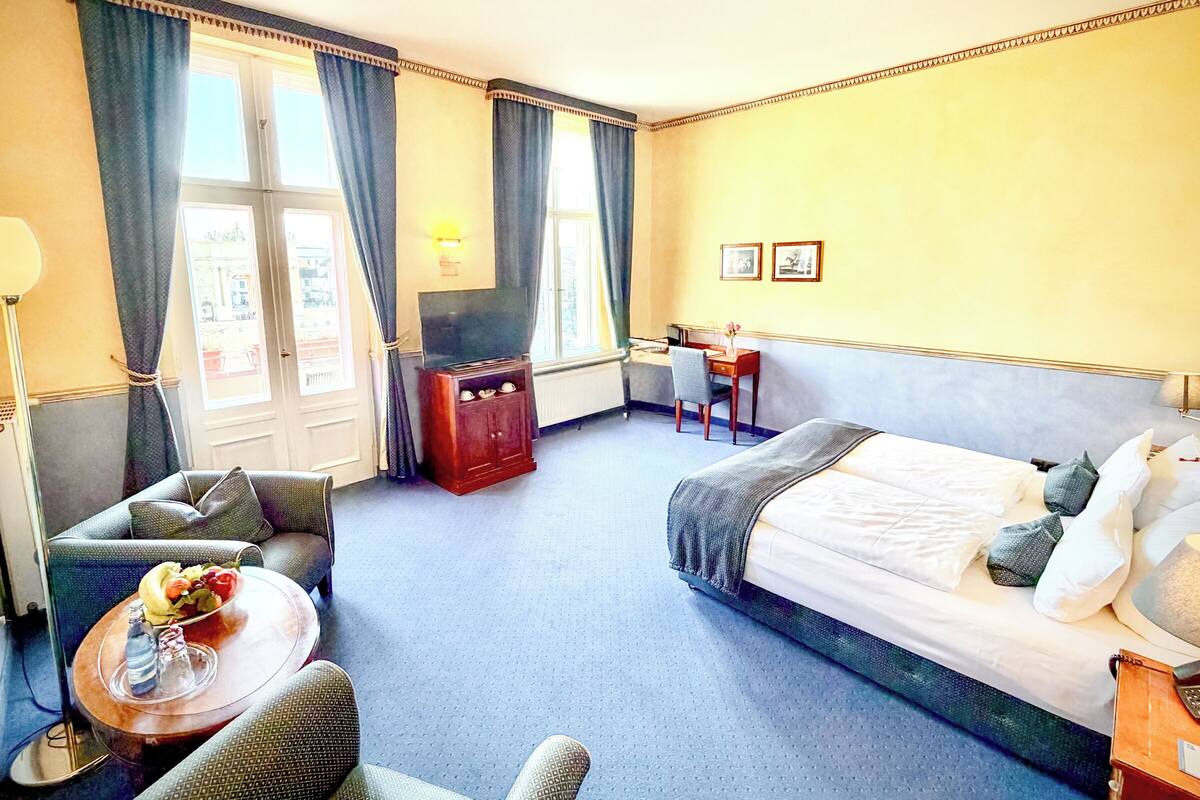 Quarto de hotel com cama, escrivaninha, cadeira, mesinha de centro com uma fruteira e televisão.