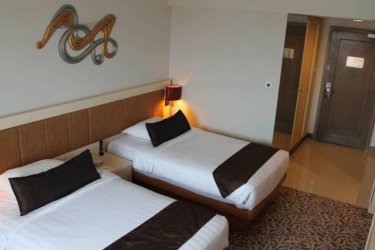 Quarto de hotel com duas camas, carpete estampado, cabeceira de madeira, luminária fixada na parede e porta com uma placa.