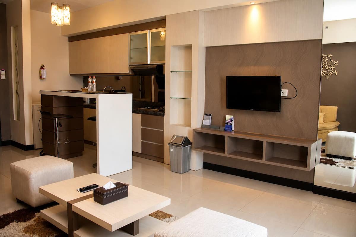 Uma sala de estar moderna com televisão de tela plana, mesa de centro, sofá e cozinha equipada com geladeira e lixeira.