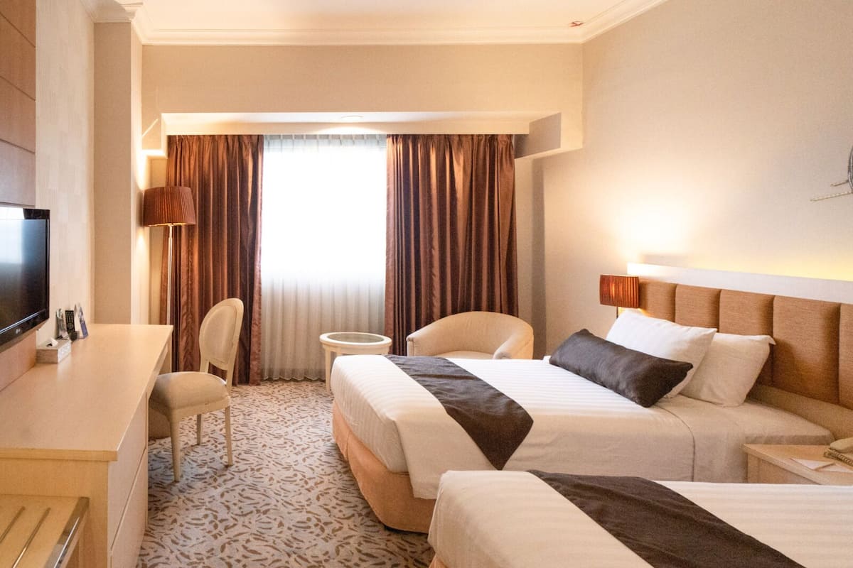 Quarto de hotel com cama, escrivaninha, cadeira, televisão e janela com cortinas.