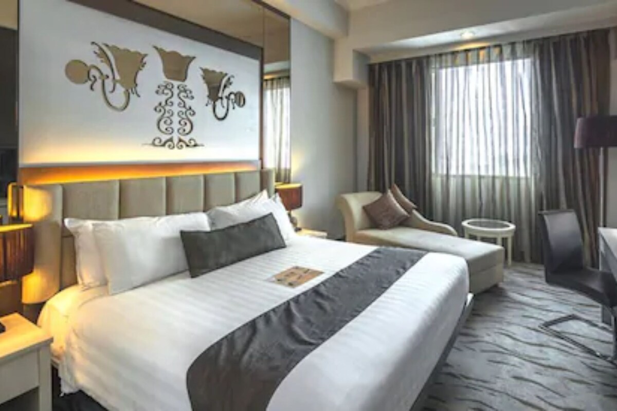 Quarto de hotel com uma cama grande, uma escrivaninha, uma cadeira, uma mesinha redonda e um sofá.