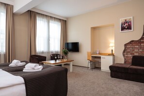 Quarto de hotel com cama, escrivaninha, televisão, cadeira e sofá.
