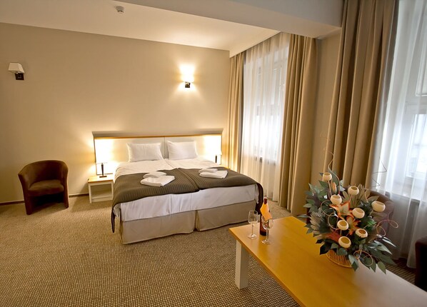 Quarto de hotel com cama, uma cadeira, mesa de cabeceira com um vaso de flores e luminária.