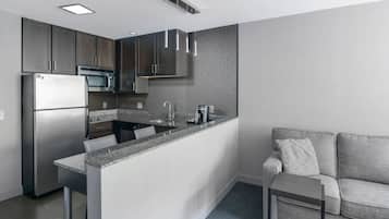 Cozinha moderna com ilha integrada, eletrodomésticos de aço inoxidável e um sofá cinza na área de estar adjacente.