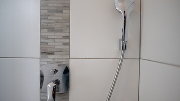 Casa de banho com chuveiro, parede revestida de azulejos e parede de destaque em tijolo.