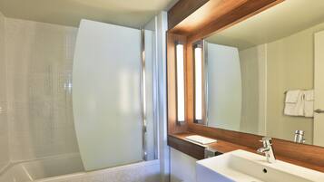 Uma casa de banho moderna com cabine de duche em vidro, toucador de madeira com lavatório e um espelho grande.