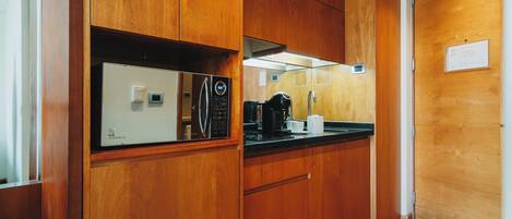 Uma cozinha compacta com armários de madeira, micro-ondas embutido e cafeteira.