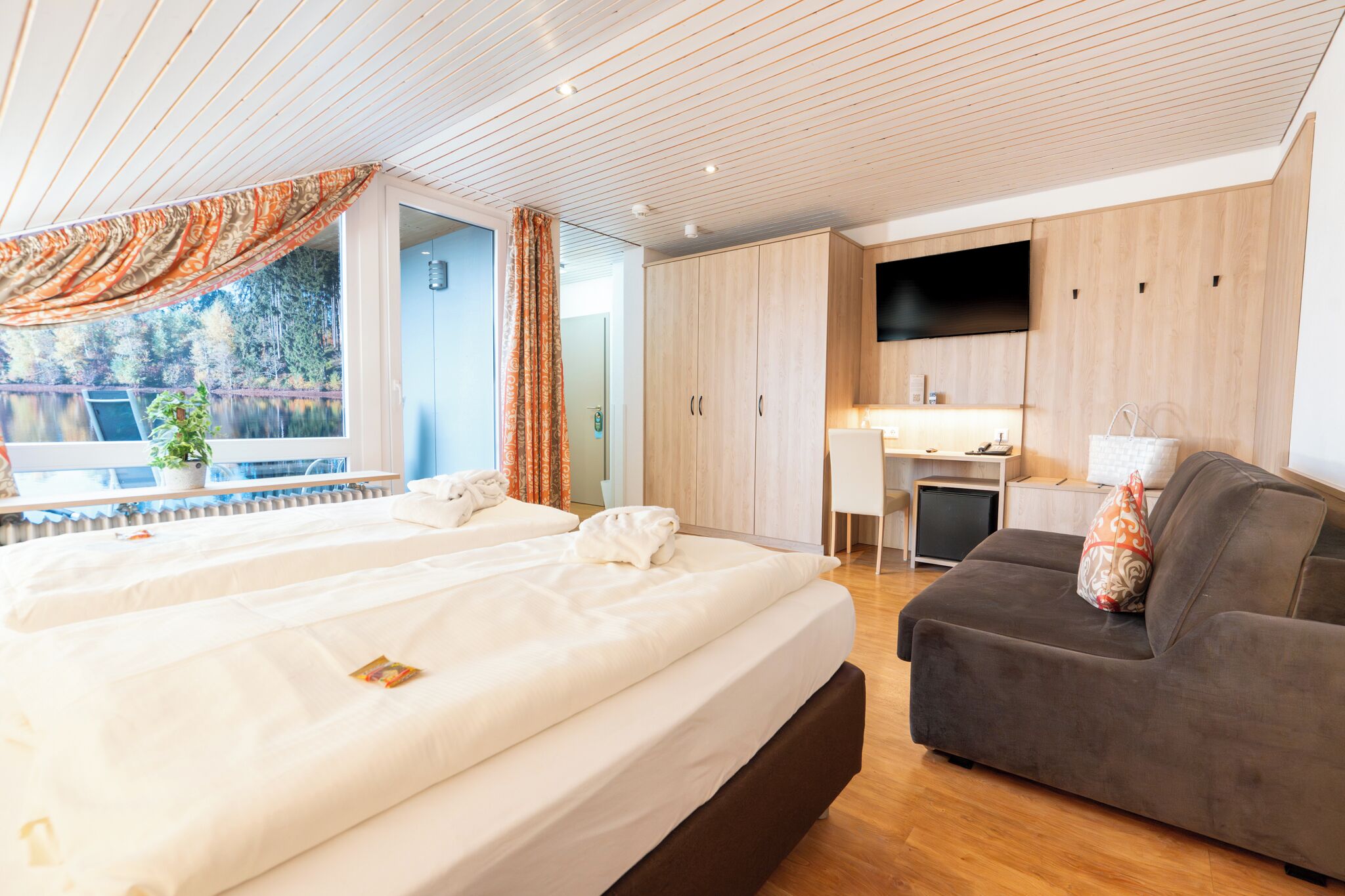 Quarto de hotel moderno com uma cama grande, um sofá, uma escrivaninha e uma televisão.