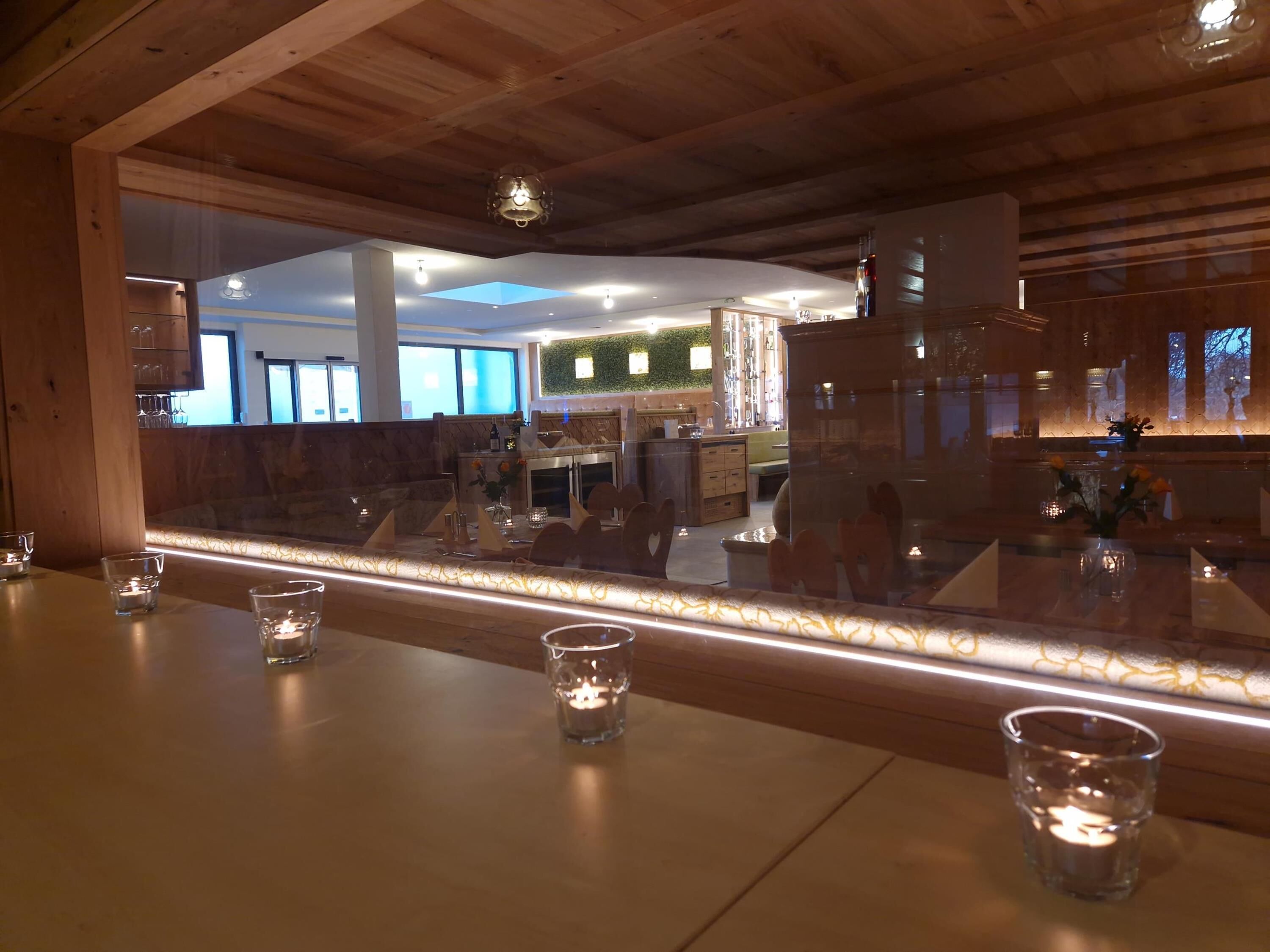 Um restaurante com interior em madeira, divisória de vidro e mesas iluminadas por velas.