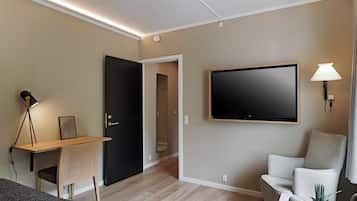Quarto de hotel moderno com escrivaninha de madeira, uma cadeira, TV de tela plana, luminária e uma área de estar confortável.