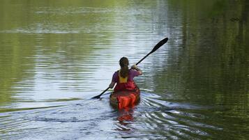 Uma pessoa pratica caiaque em um rio calmo, rodeada por vegetação.