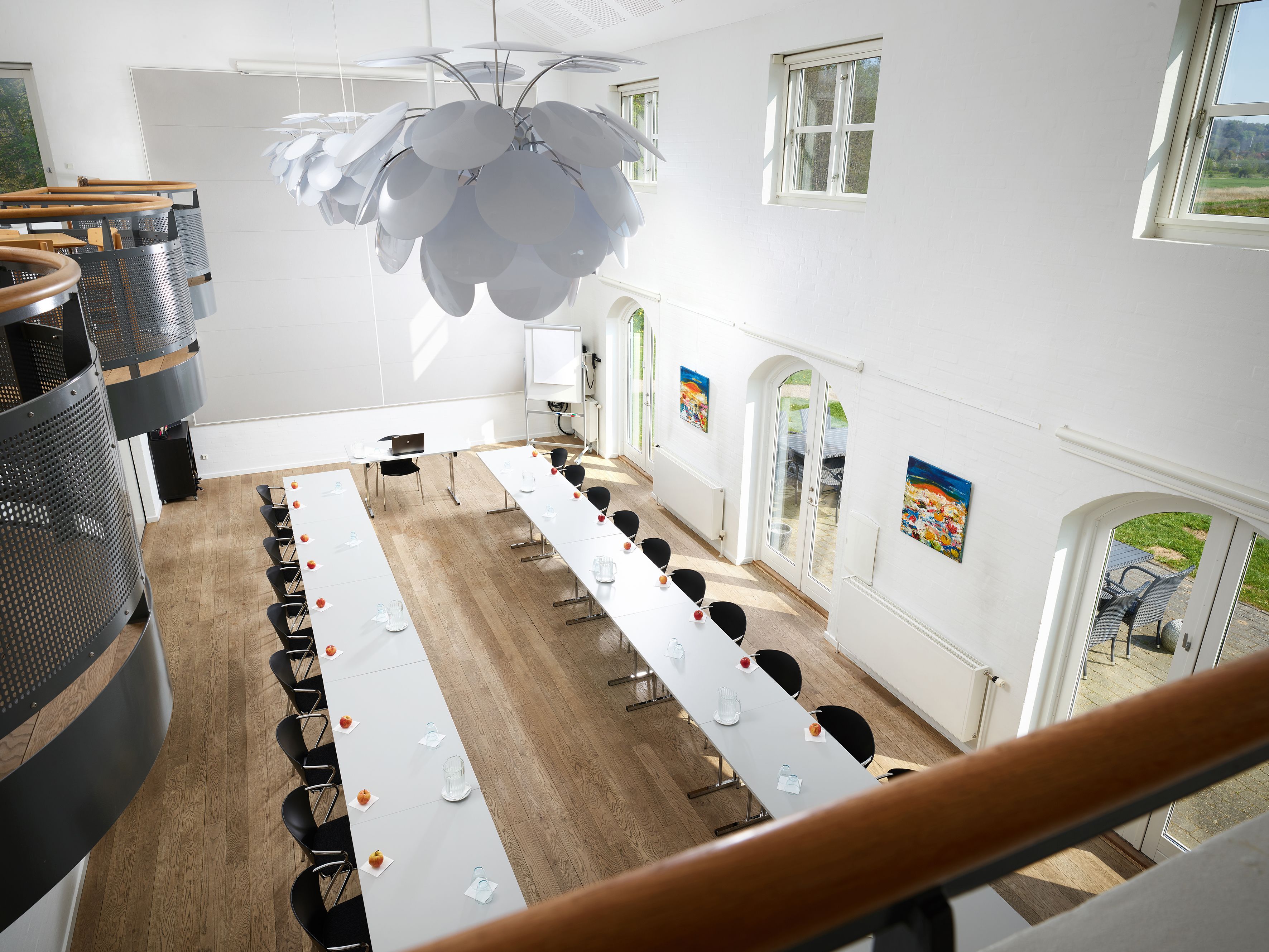 Sala de conferências com mesas compridas, cadeiras e um lustre moderno.