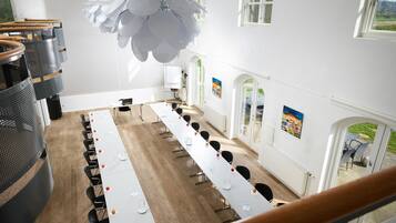 Sala de conferências com mesas compridas, cadeiras e um lustre moderno.