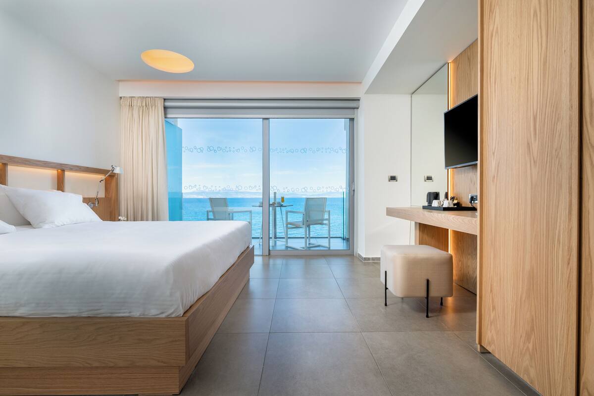 Quarto de hotel moderno com uma cama grande, uma mesa, uma TV e uma varanda com vista.