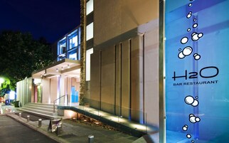 Um bar e restaurante moderno com fachada de vidro e uma placa com a inscrição "H2O BAR RESTAURANT".