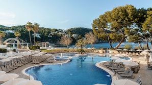 Área de piscina com espreguiçadeiras e guarda-sóis, rodeada por árvores e com vista para um corpo de água.