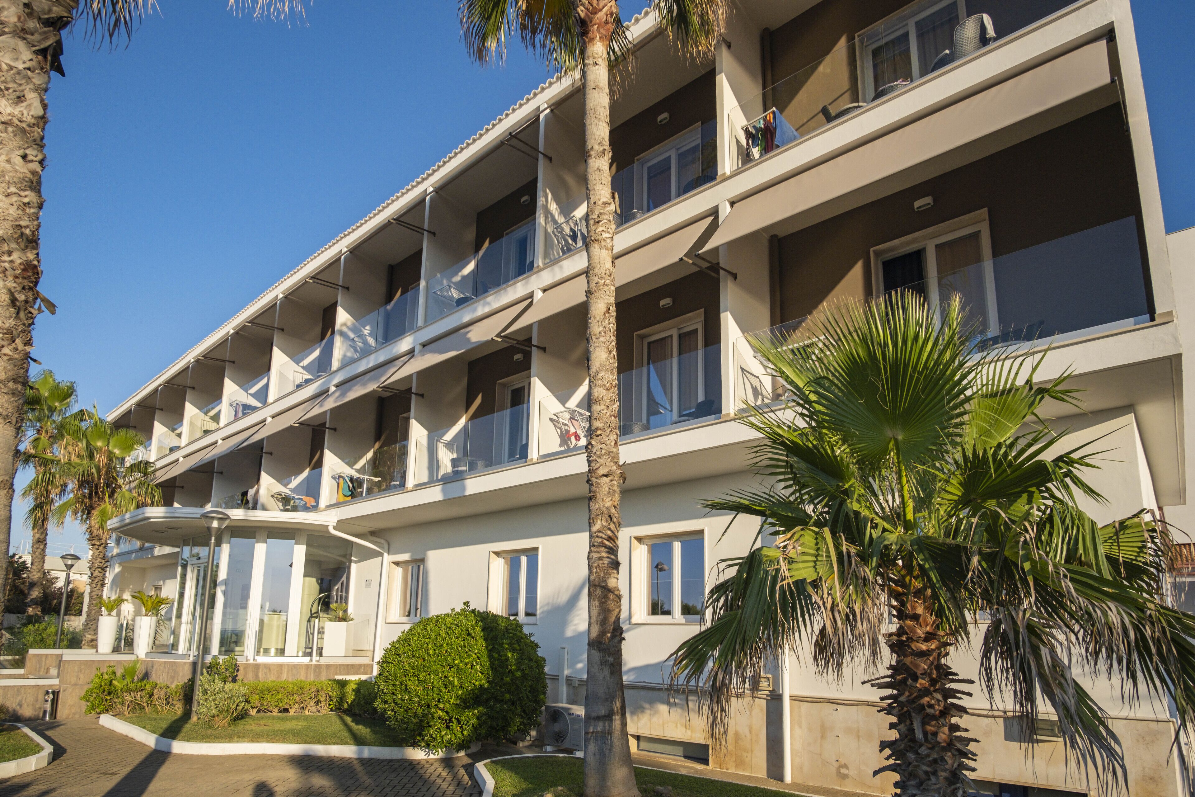 Um hotel com vários andares, varandas, palmeiras e um jardim bem cuidado.
