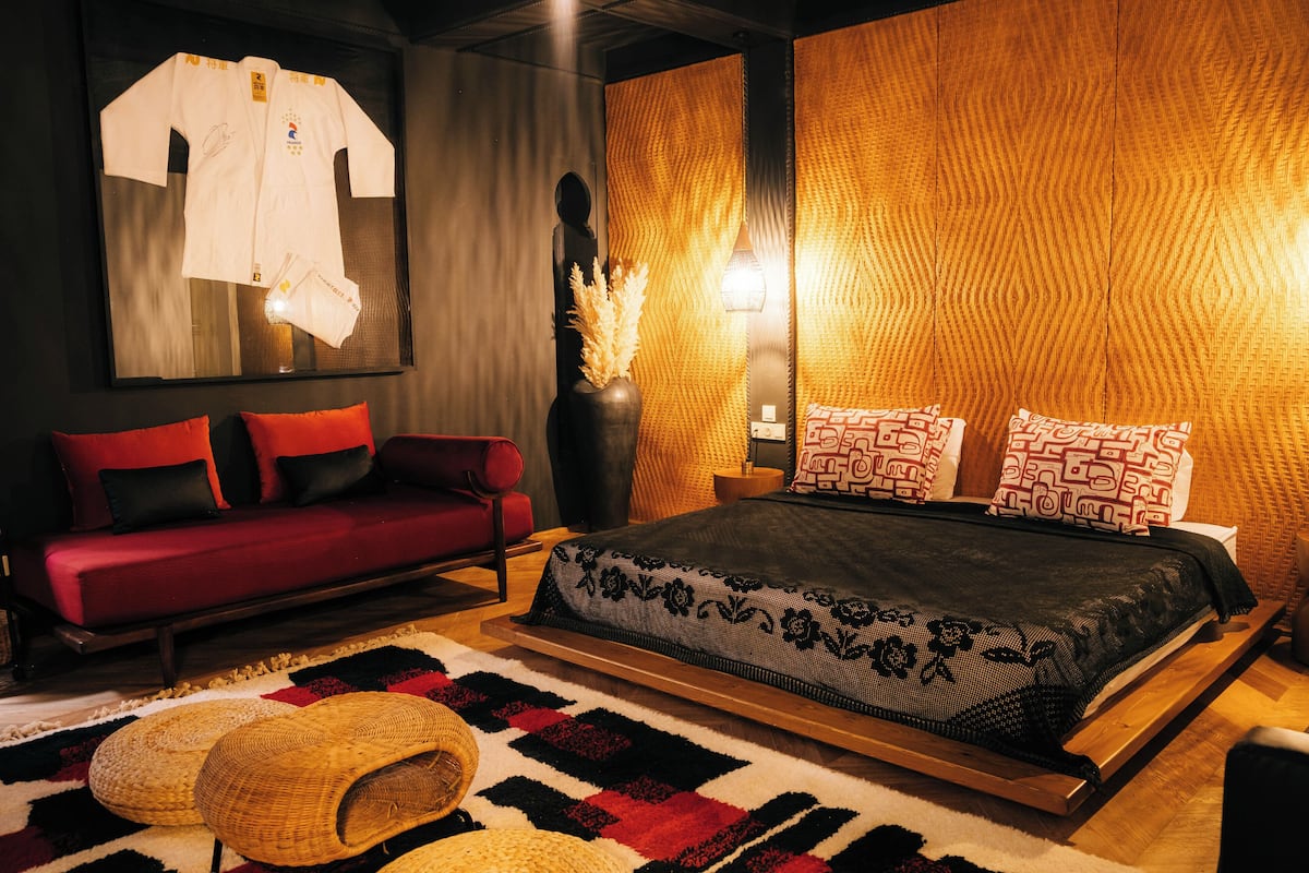 Quarto com cama, sofá vermelho, espelho grande e um vaso decorativo.