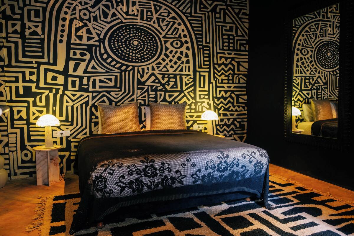 Um quarto com parede estampada, cama com colcha florida, duas luminárias e um tapete.