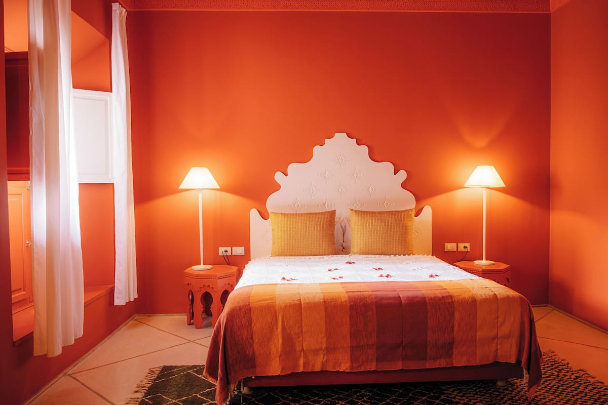 Quarto com cama, duas luminárias de cabeceira, mesa de cabeceira e cortina.