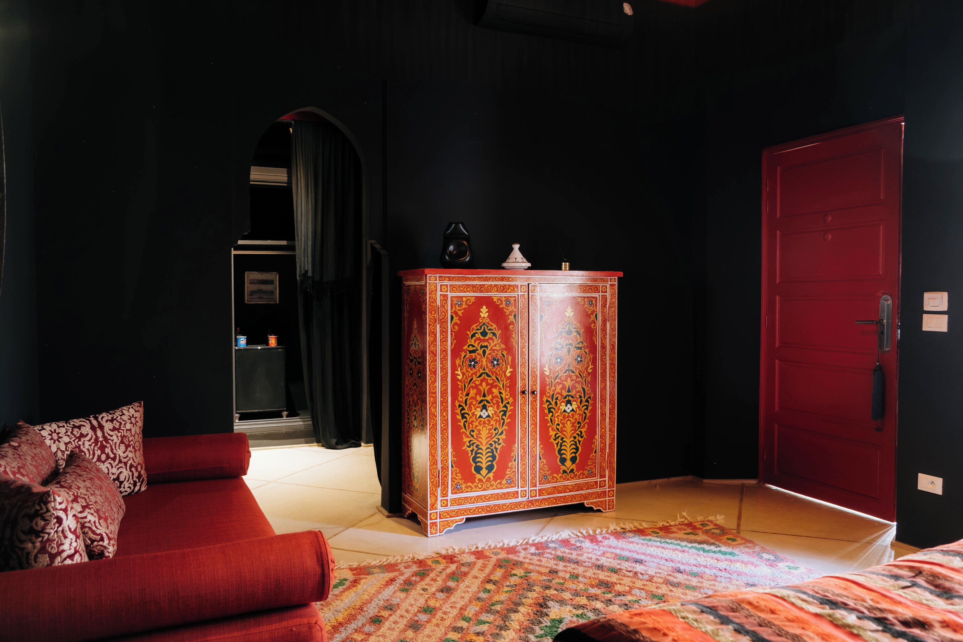Quarto com sofá vermelho, tapete estampado, aparador decorativo e porta vermelha.