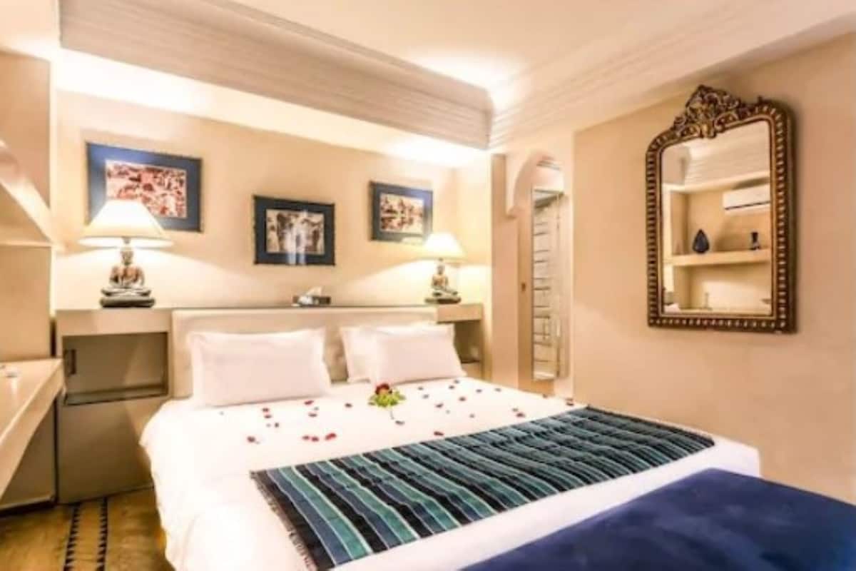 Quarto de hotel com cama, mesas de cabeceira, luminárias, quadros na parede e um espelho.