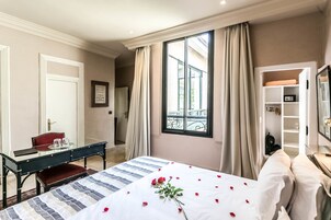Quarto de hotel com cama, escrivaninha, cadeira, guarda-roupa e janela com cortinas.
