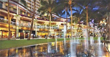 A atrium de hotel com vários níveis, com um elemento central de água, palmeiras e diversas lojas no andar térreo.